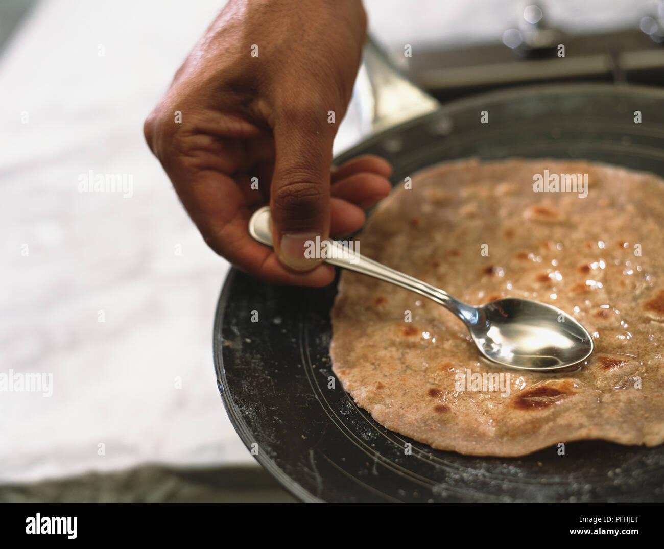 Putting oil on to Chapati bread on a hot plate Stock Photo - Alamy