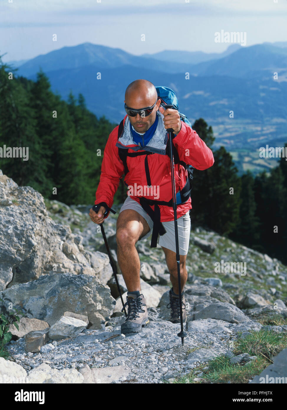Man ascending a rocky incline using trekking poles Stock Photo - Alamy