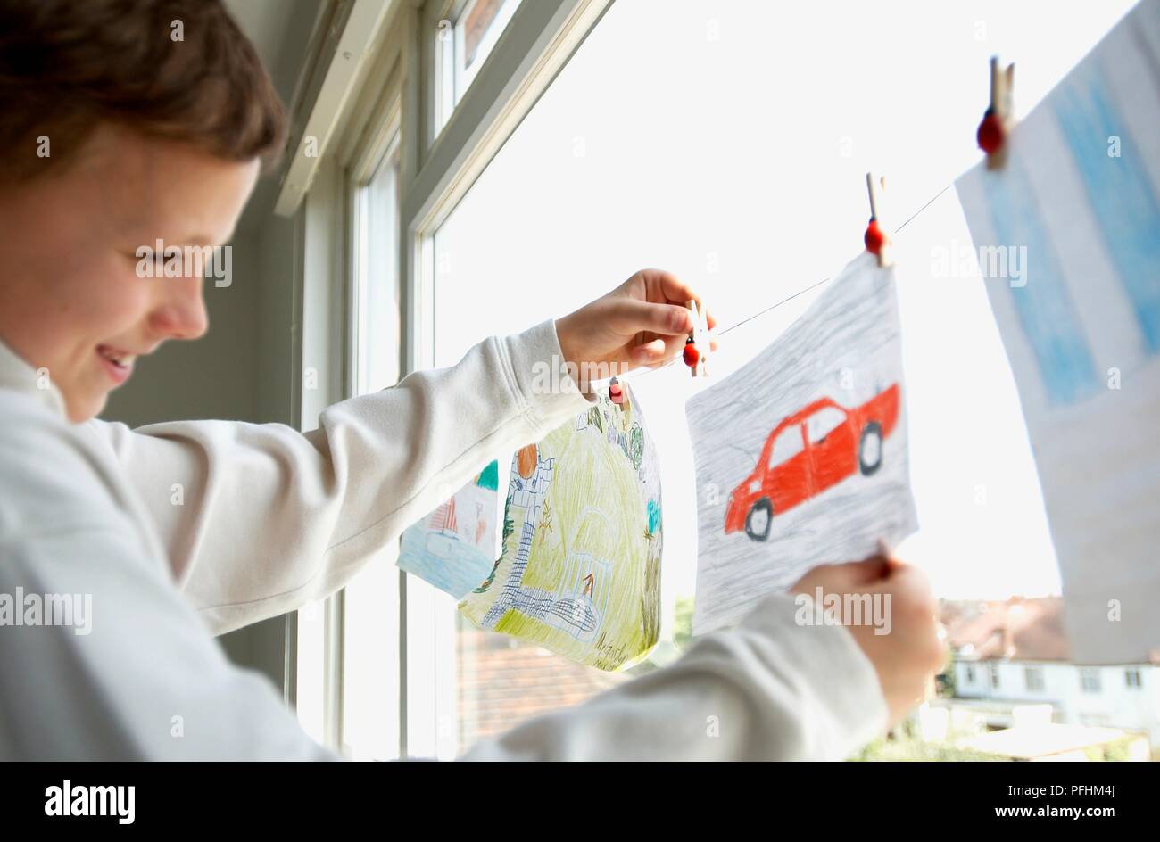 Smiling boy attaching drawing of red car to line of string across ...