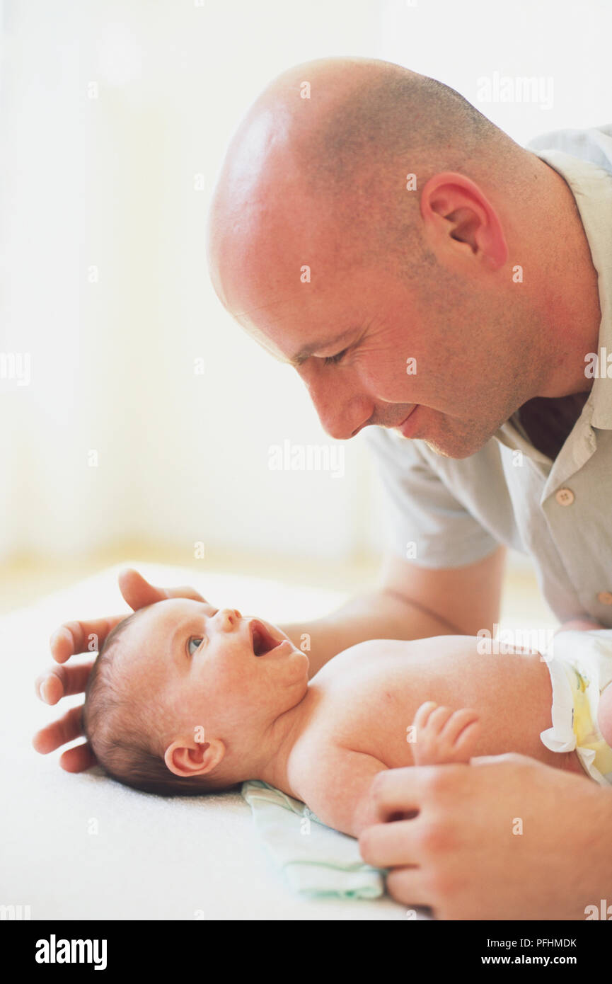 Smiling man leaning over young gaping baby lying on his back, side view ...