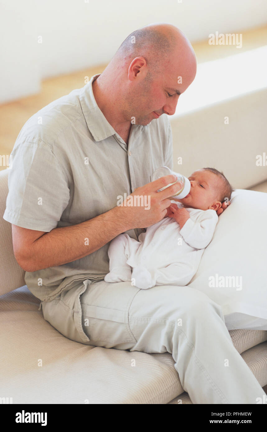 Man bottle-feeding a young baby, side view Stock Photo - Alamy