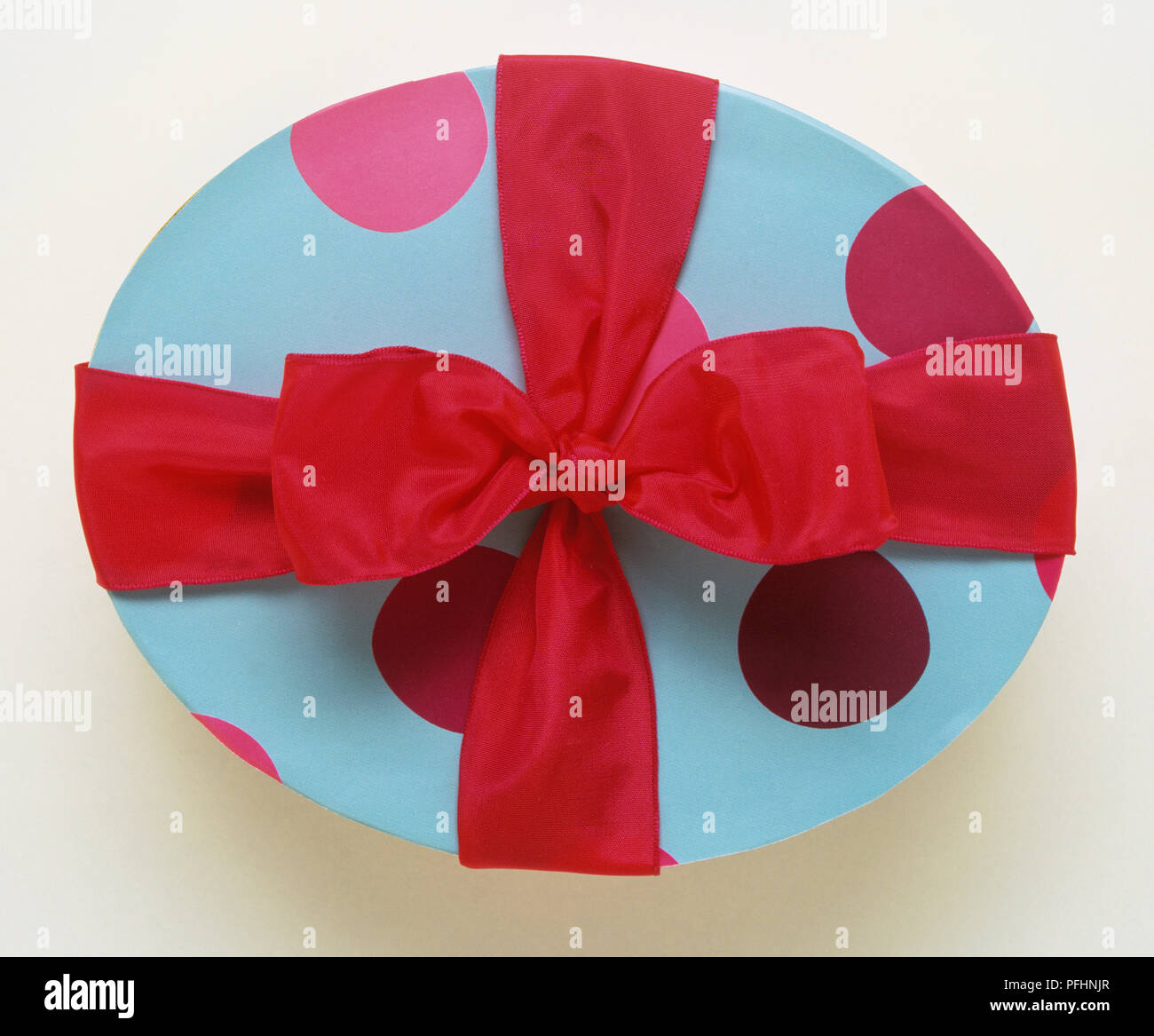 An oval gift wrapped in blue spotted paper and tied with red ribbon ...