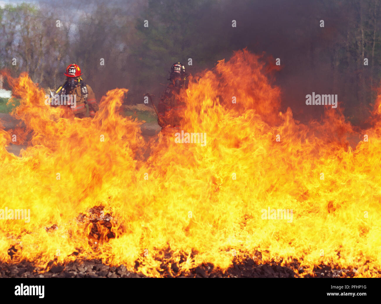 Two firefighters standing behind fierce flames of wall of fire Stock ...