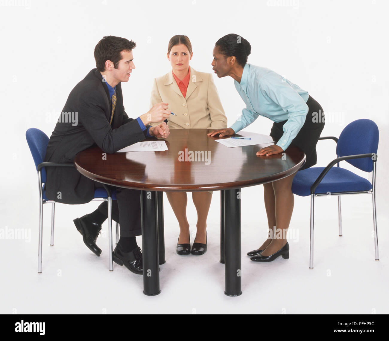 Man and two women having heated debate around meeting table, one woman ...