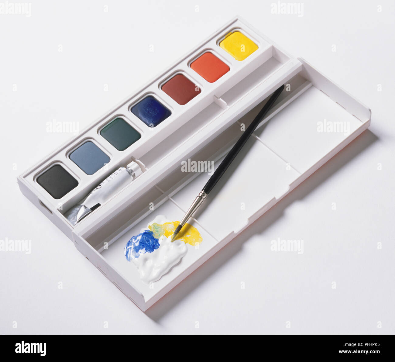 Watercolour paint box containing a range of colours and a brush next to ...