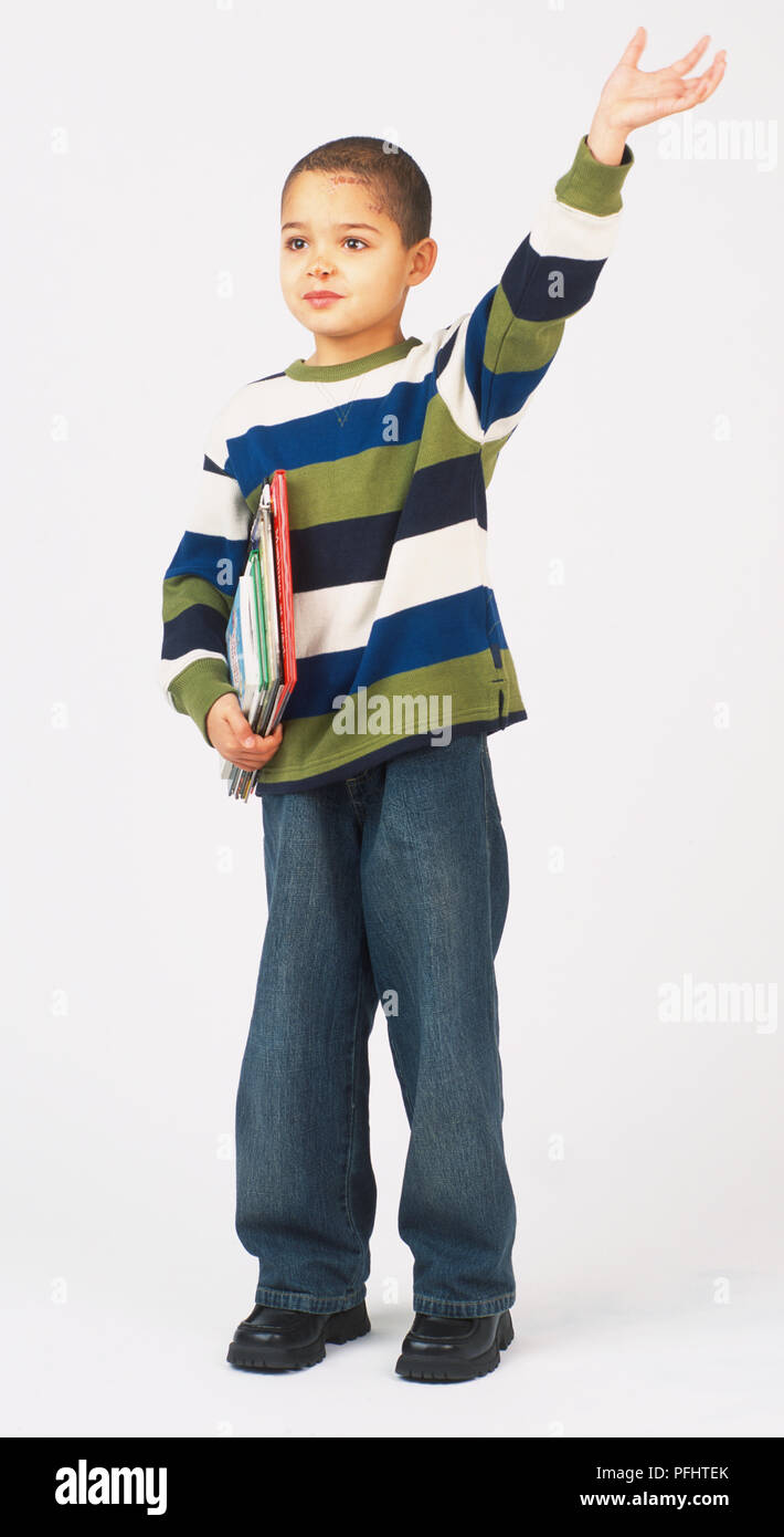 Standing boy holding books under one arm and raising the other in a ...