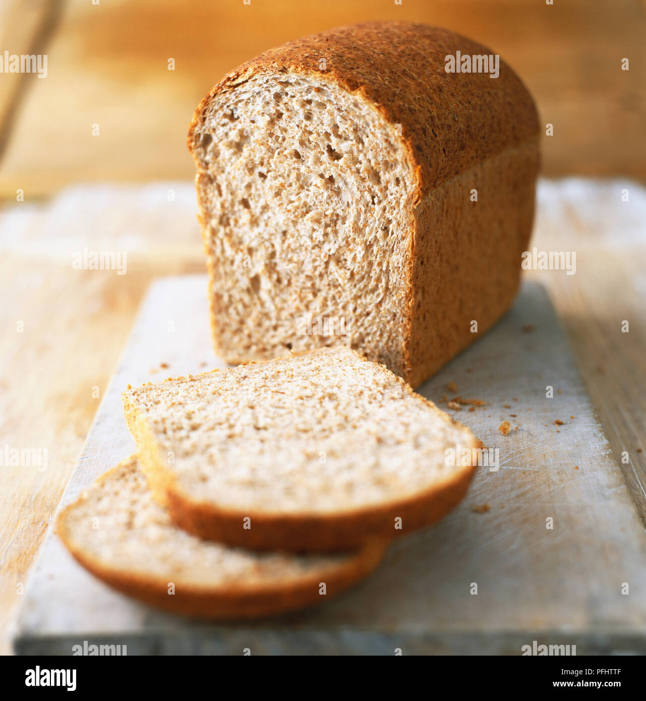 Loaf of brown bread on wooden chopping board with two cut slices laying ...