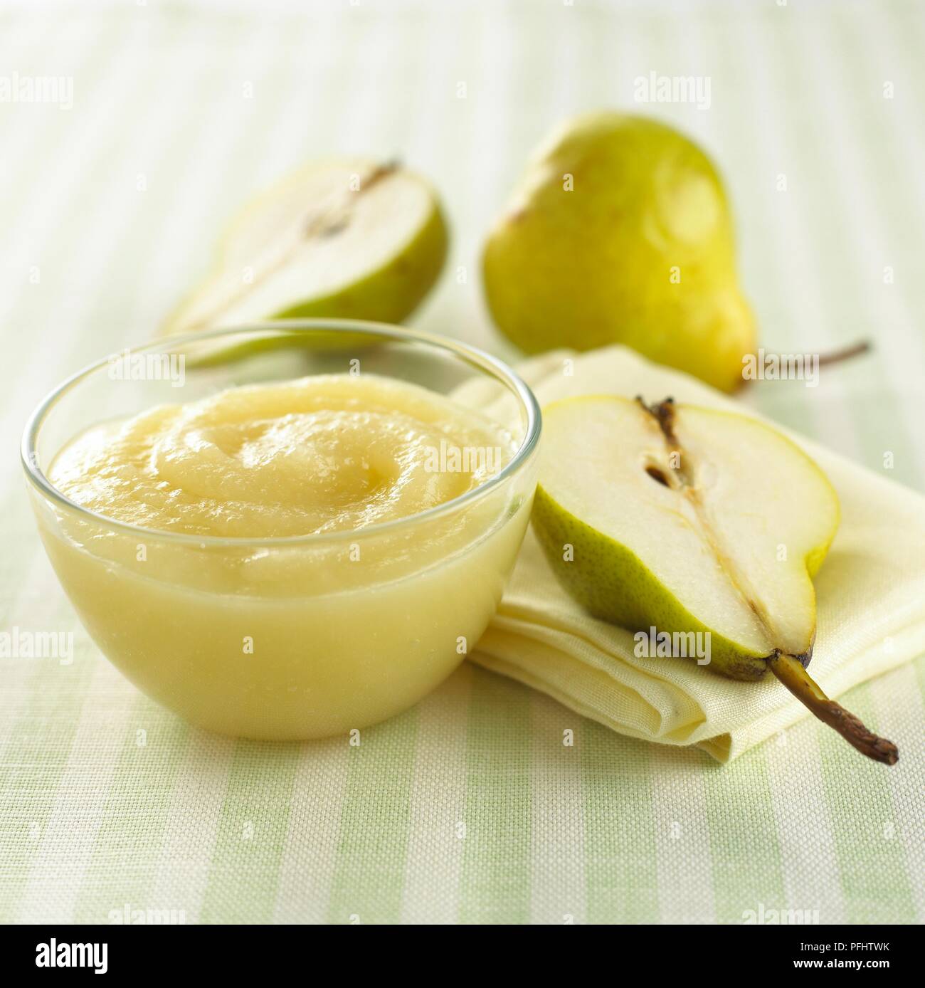 Glass dish filled with pear puree, whole pear and pear halves on napkin ...