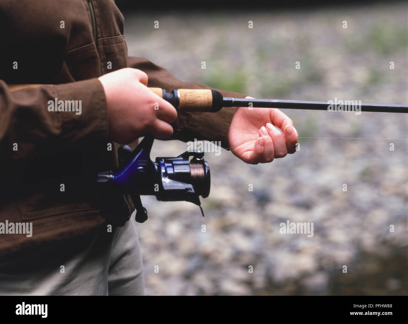 Hands holding fishing rod and pulling its line close to the reel, side ...