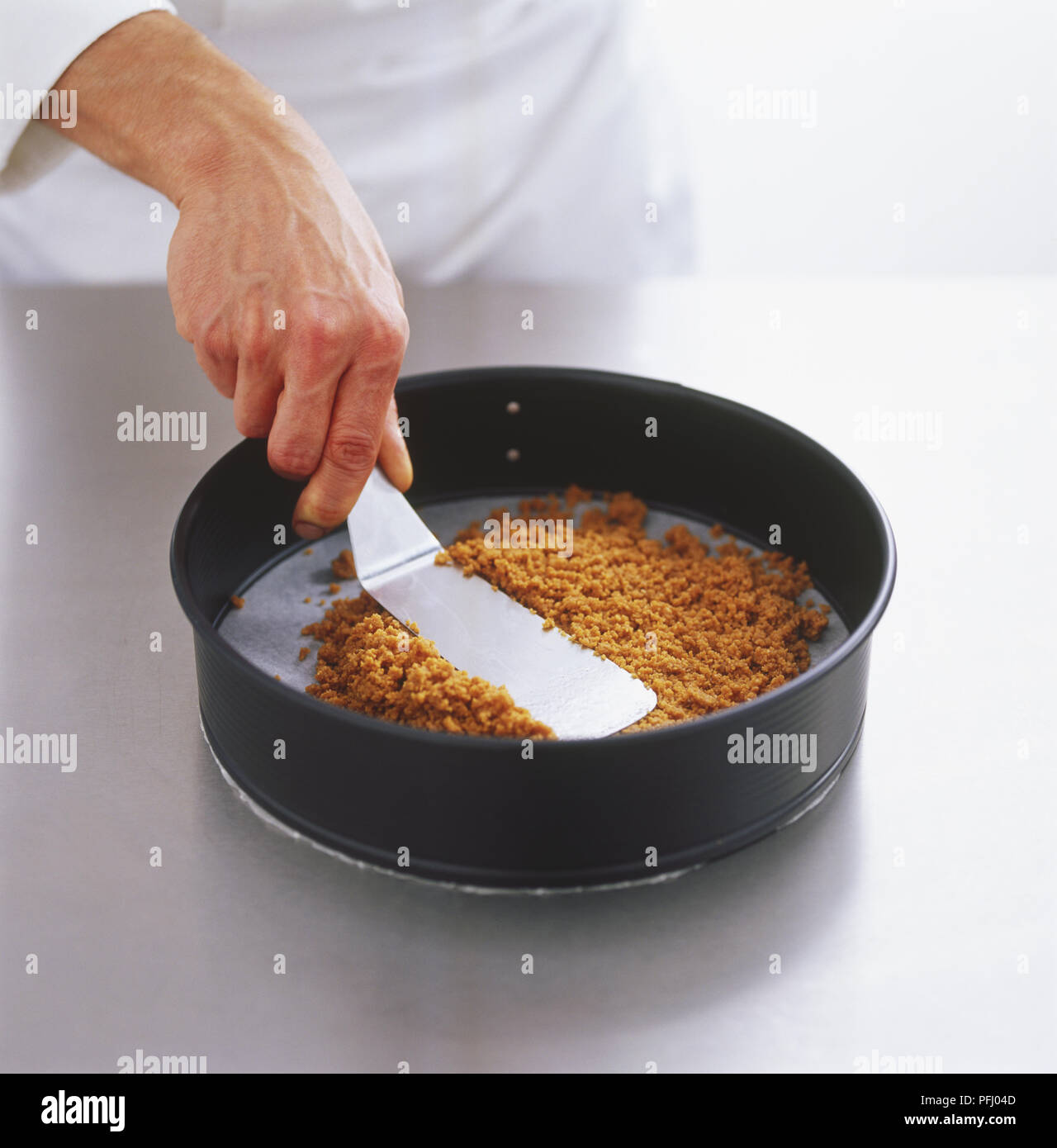 Using a spatula to press bread crumbs into bottom of cake tin Stock ...
