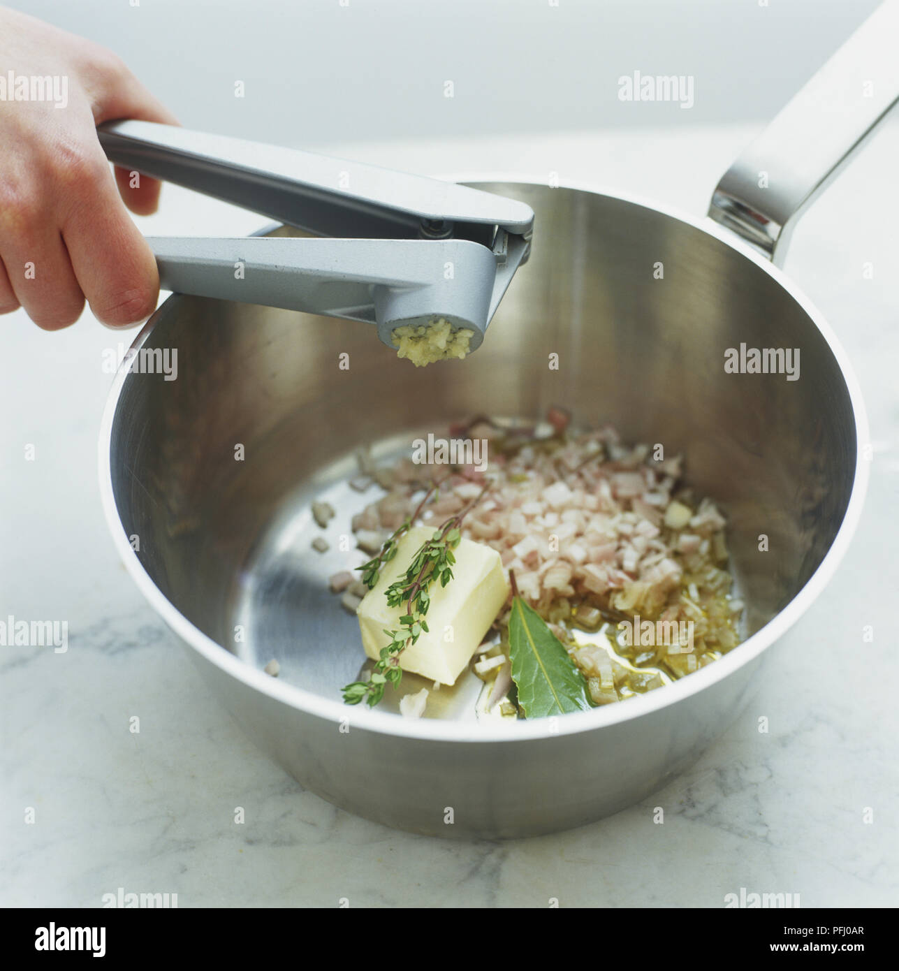 Garlic being crushed into saucepan containing butter, oil, chopped ...