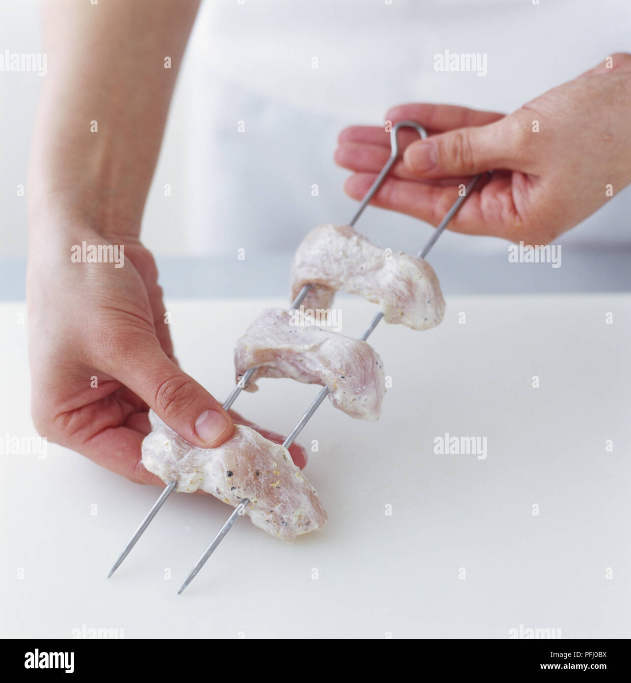 Threading chicken strips onto pair of skewers Stock Photo - Alamy