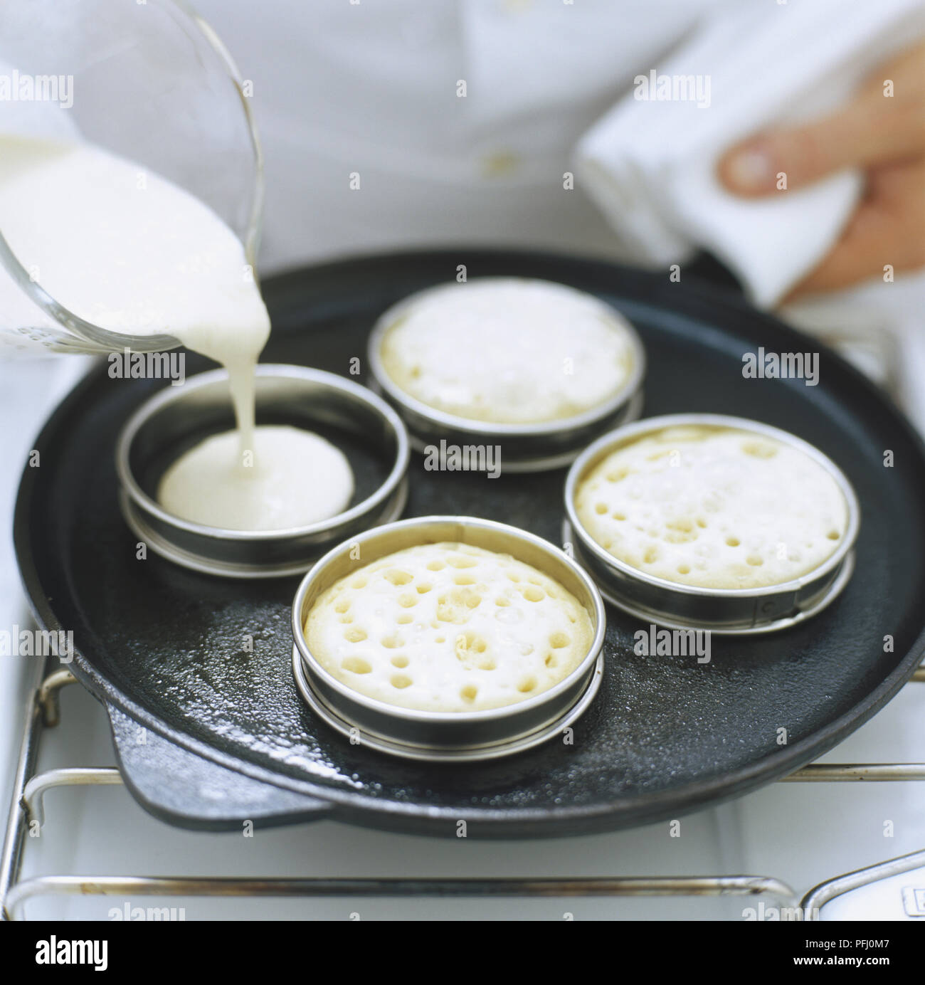 Crumpet mixture being poured into griddles on frying pan, high angle ...