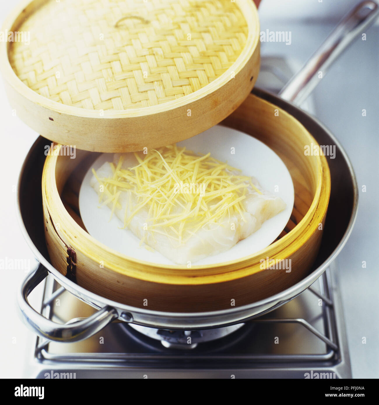 White fish fillet topped with shredded ginger root in bamboo steamer ...