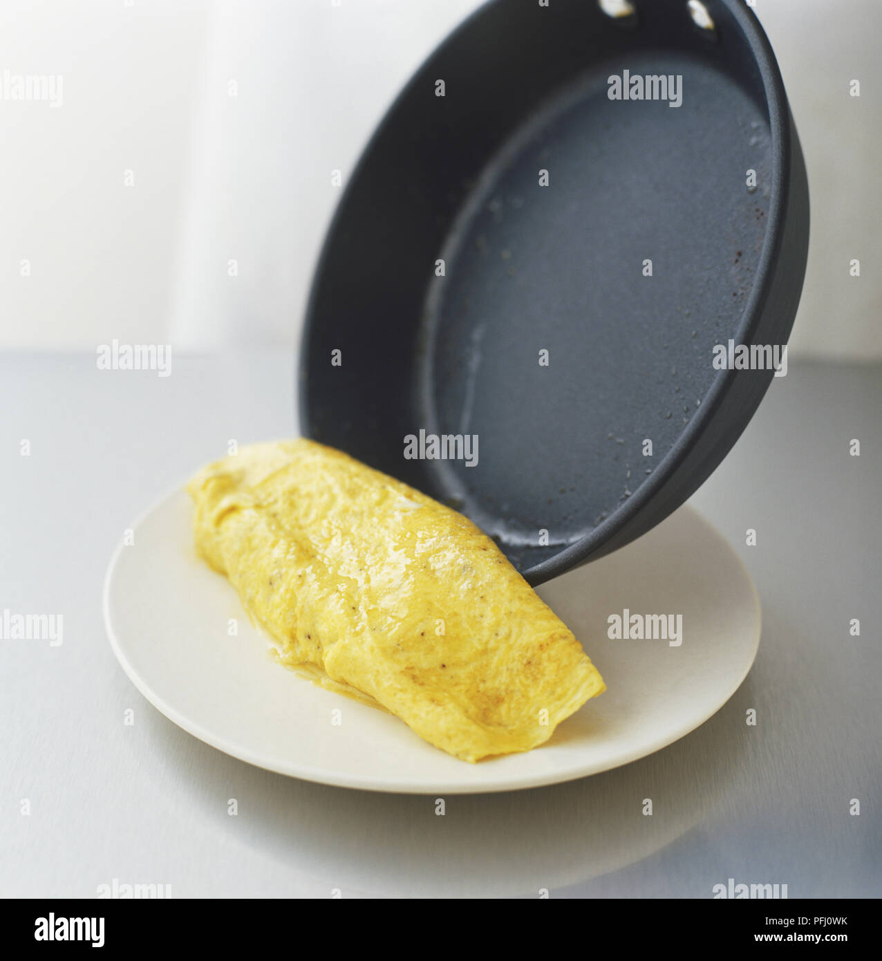 Omelette being tipped from frying pan onto plate, side view Stock Photo ...