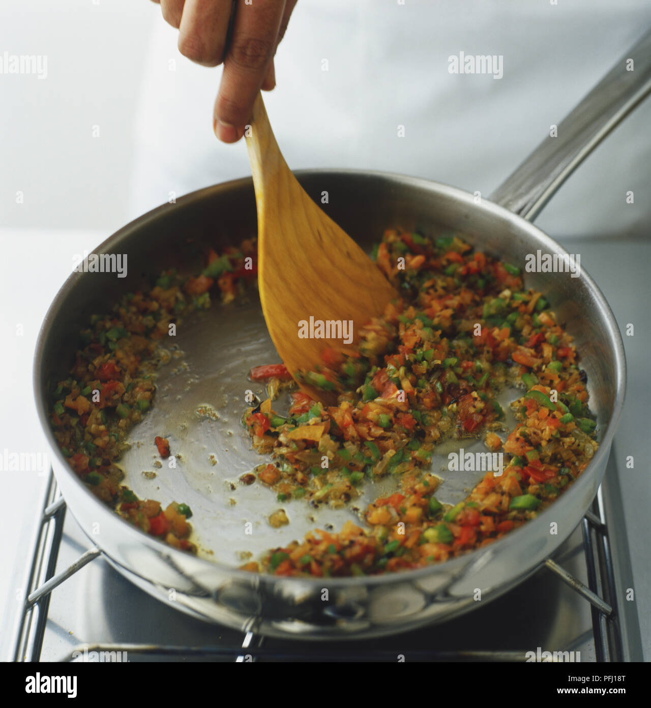 Using wooden spoon to stir mixture of finely chopped onions, tomatoes ...