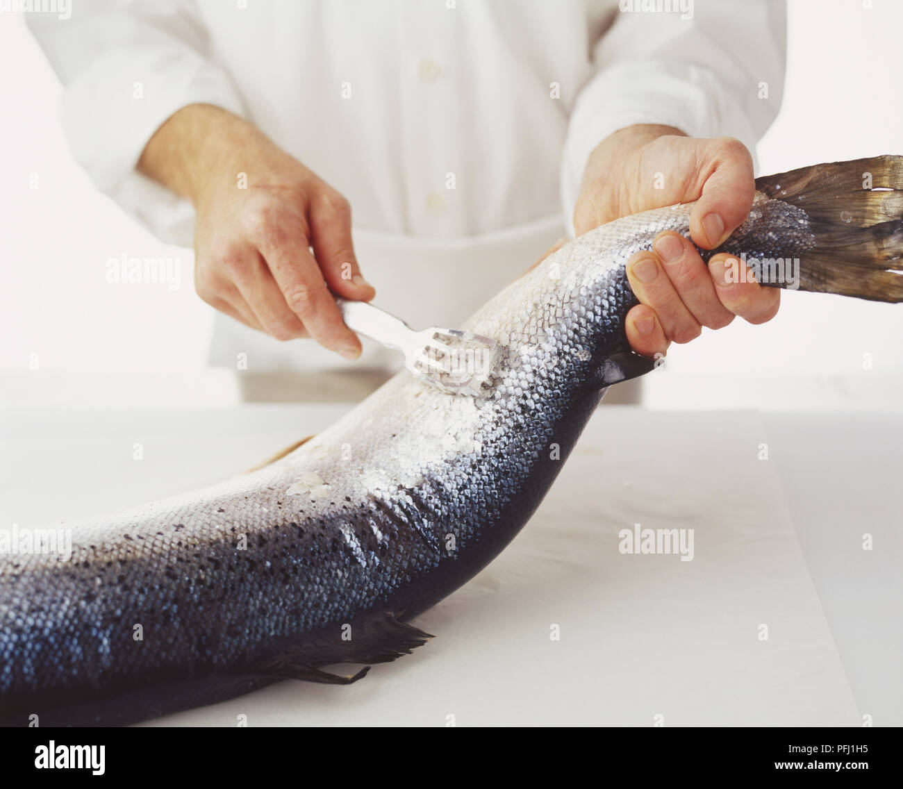 Holding the tail of a salmon and using a fork to scrape off scales ...