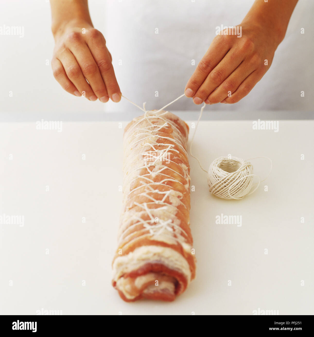 Rolled pork belly being tied with string, front view Stock Photo - Alamy
