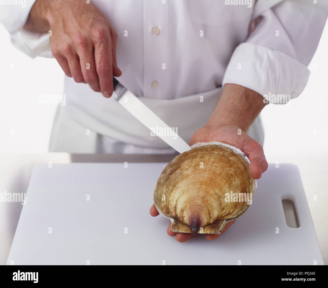 Scallop being opened with sharp knife over chopping board, front view ...