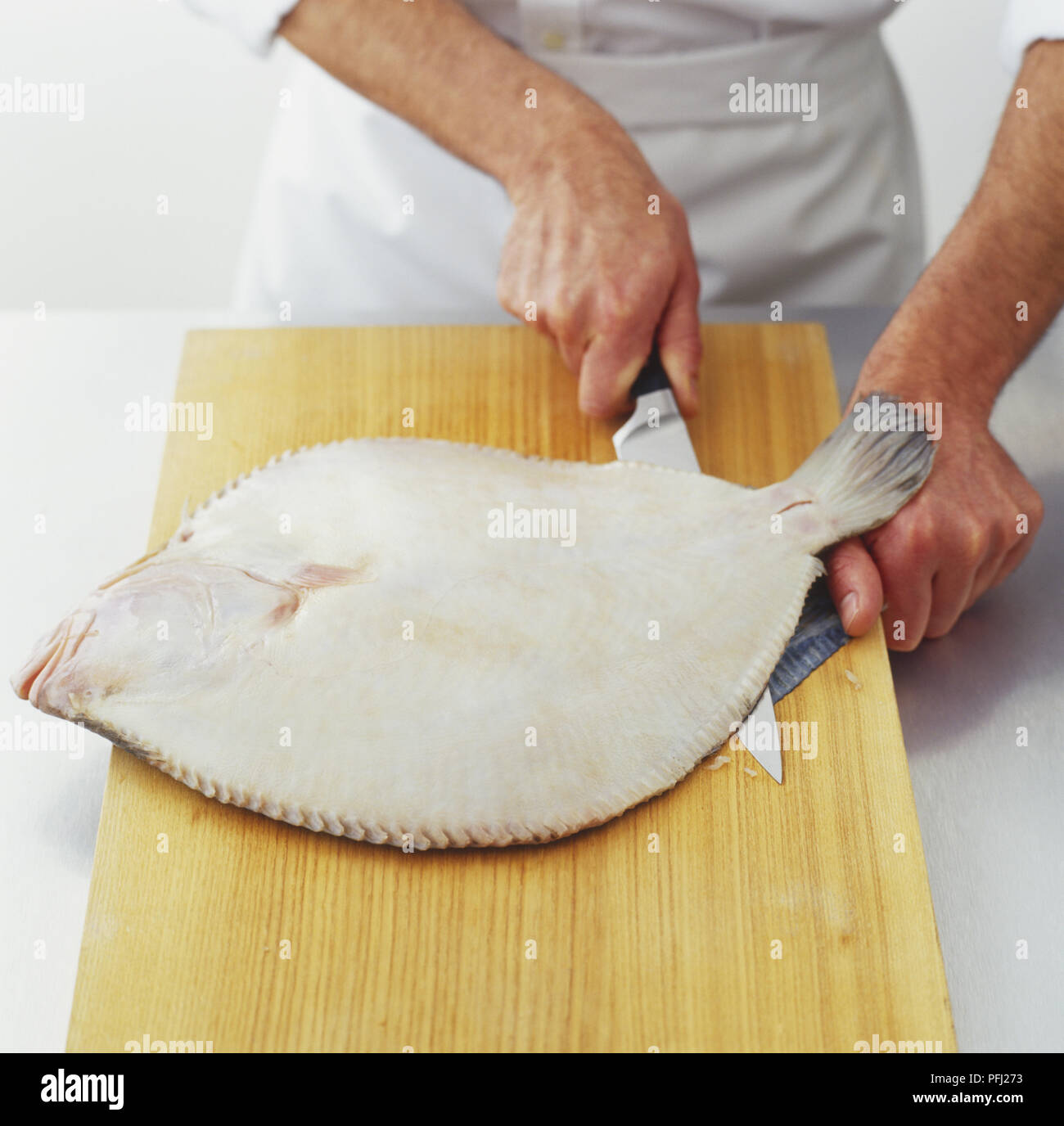 Flat fish being skinned with a knife on wooden chopping board, high ...