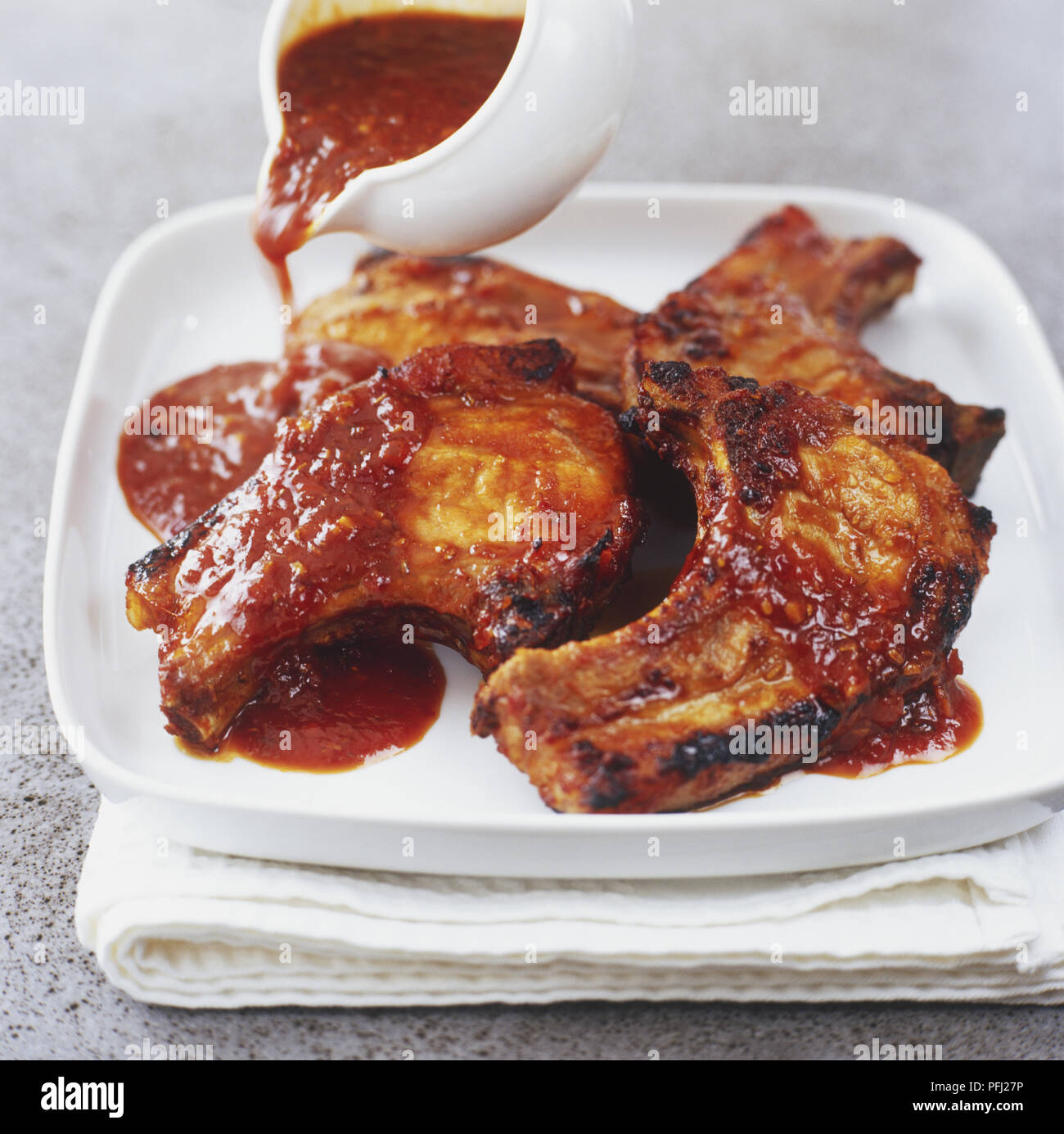 Pouring chilli marinade over grilled pork chops on a square serving ...