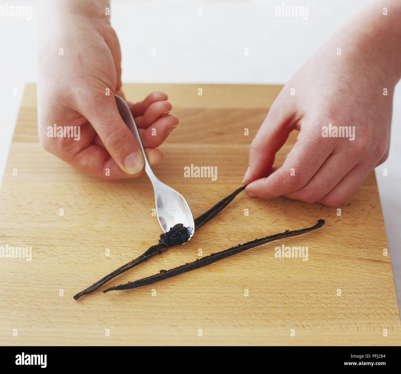Seeds being scraped out of split vanilla pod with a spoon, high angle ...