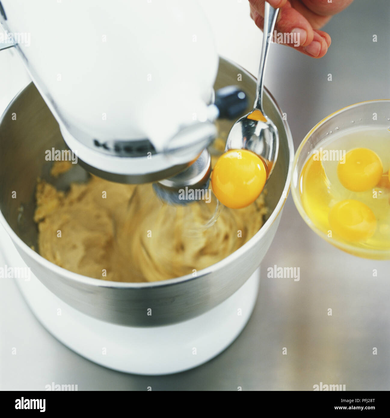 Raw egg yolks being spooned into mixture in electric mixer container ...