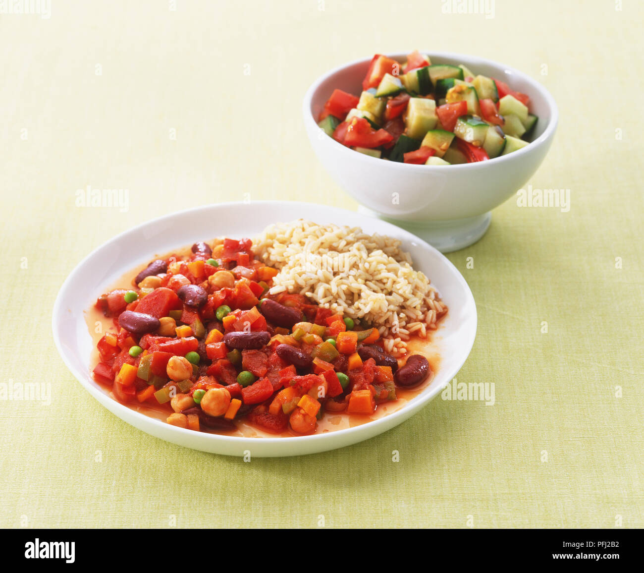 Dish of mixed beans and vegetable chilli with brown rice, and bowl of ...