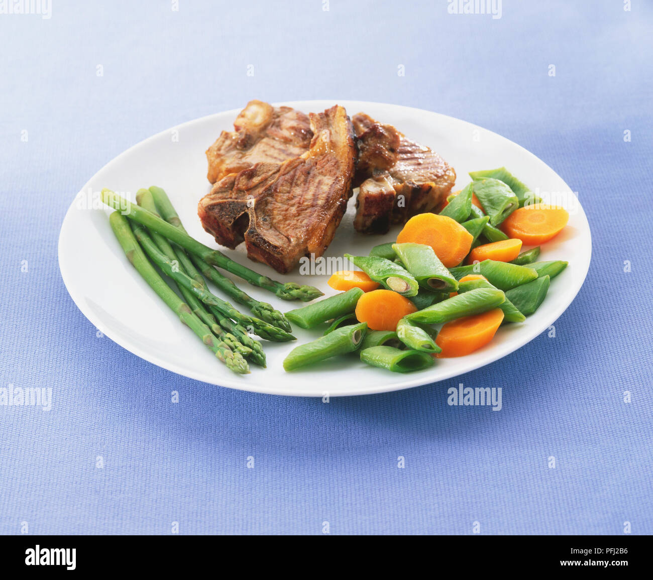 Two grilled lamb chops on dish with asparagus, runner beans, and ...