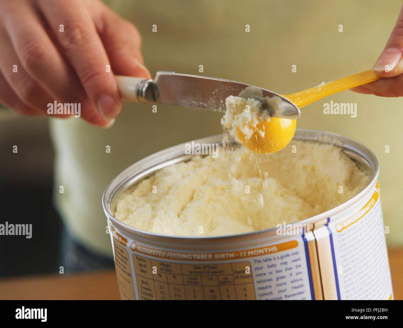Using knife to level off yellow plastic scoop full of infant formula ...