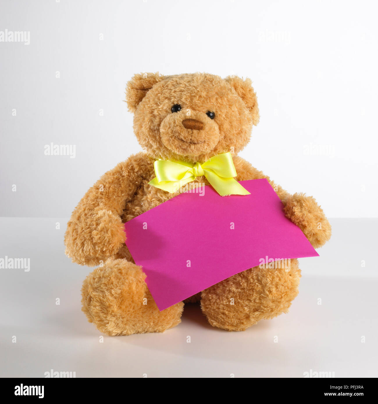Teddy bear with yellow ribbon tied around neck holding purple envelope ...