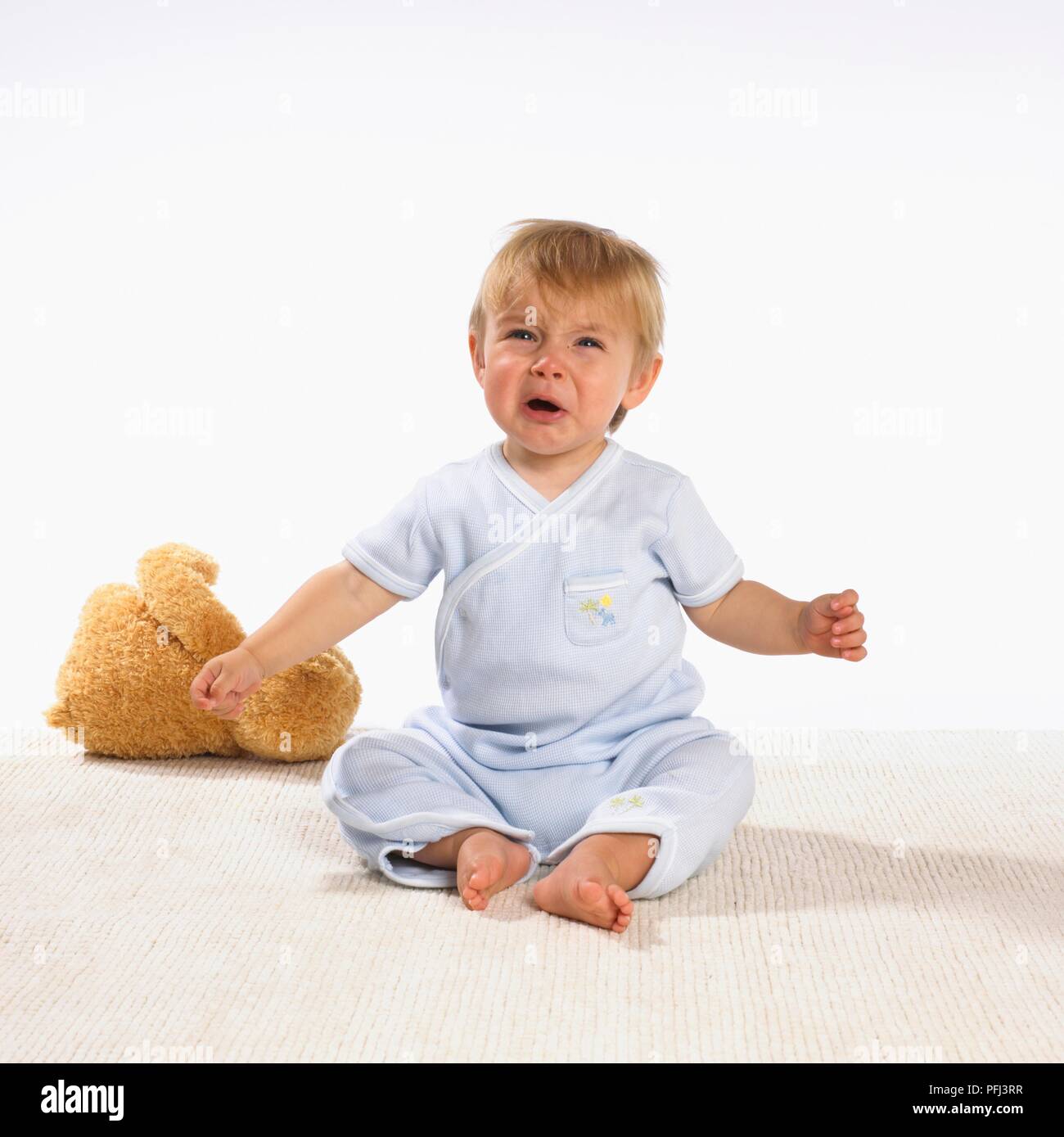 Baby boy in pyjamas crying, teddy bear at side Stock Photo - Alamy