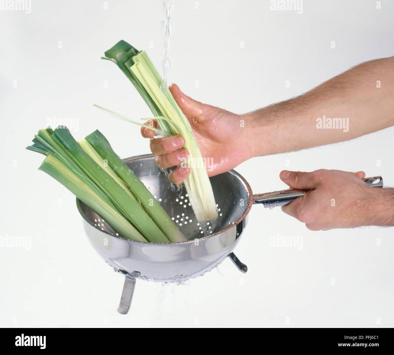 Holding leeks under running water over colander Stock Photo - Alamy
