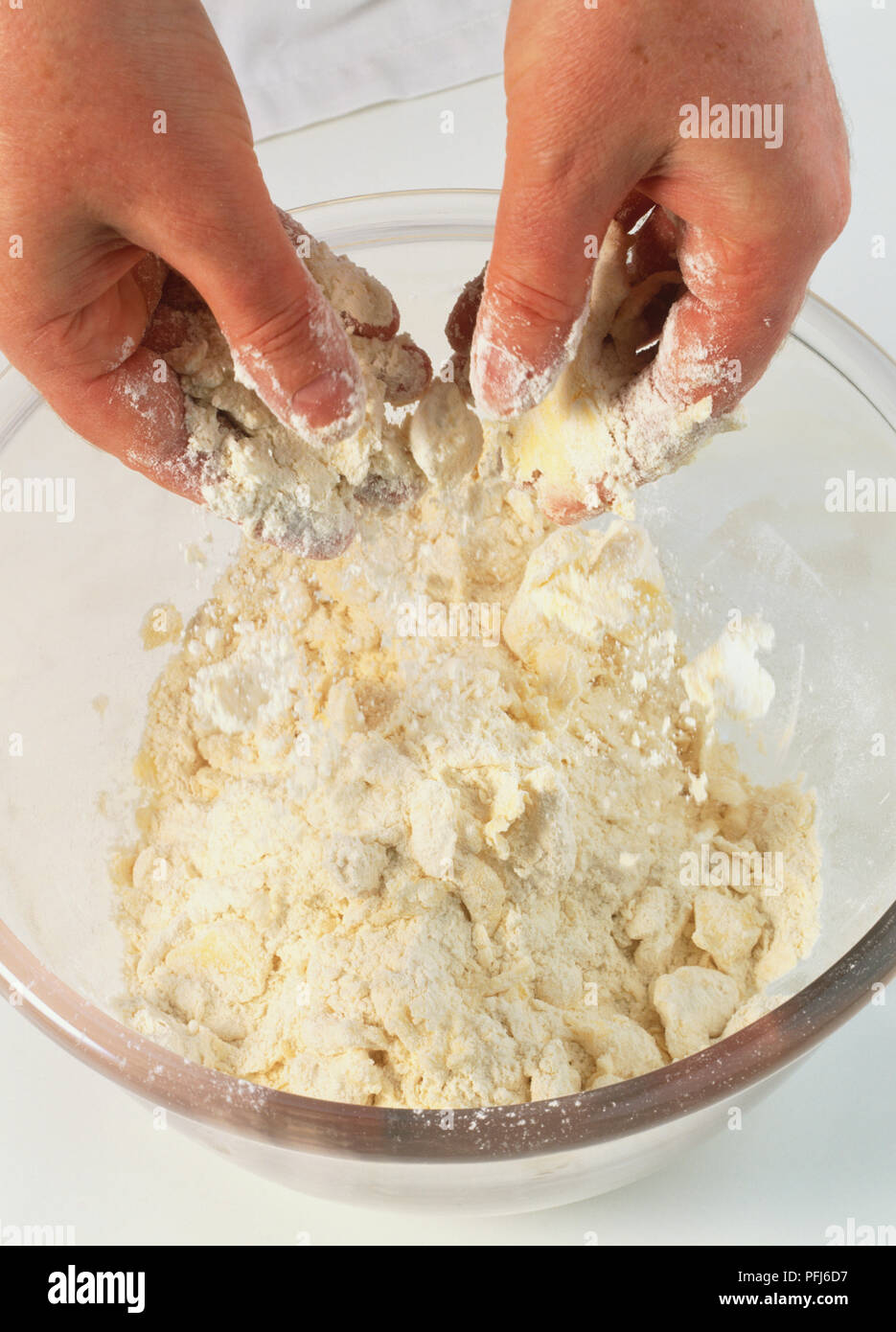 Pair of hands rubbing fat and flour together in a glass bowl, close up ...
