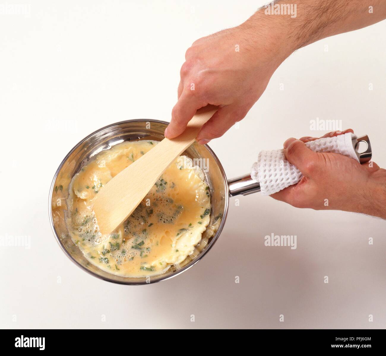 Holding hot handle of frying pan with cloth and using wooden spatula to ...