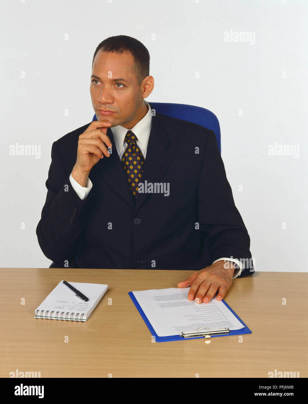 Man in business suit sitting at a desk with his hand on his chin, pen ...
