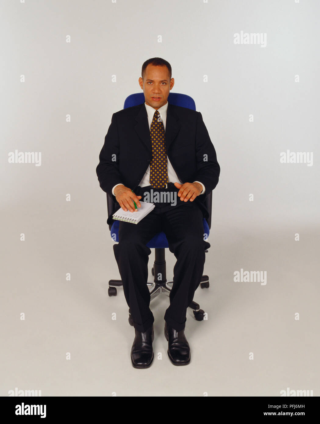 Man in a business suit and tie sitting in office chair with a notepad ...