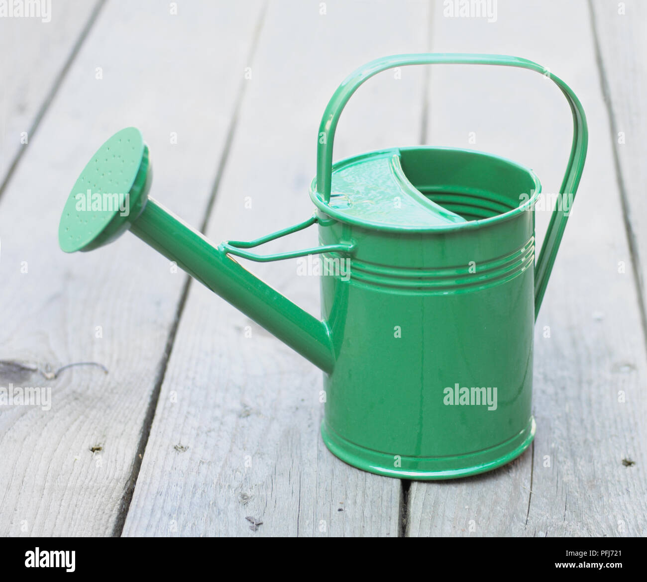 Green watering can on garden decking, side view Stock Photo - Alamy