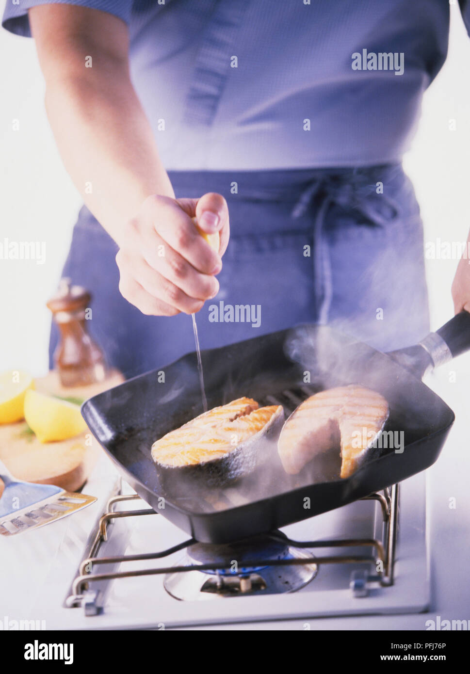 Lemon being squeezed over fish fillets grilling in pan, elevated view ...
