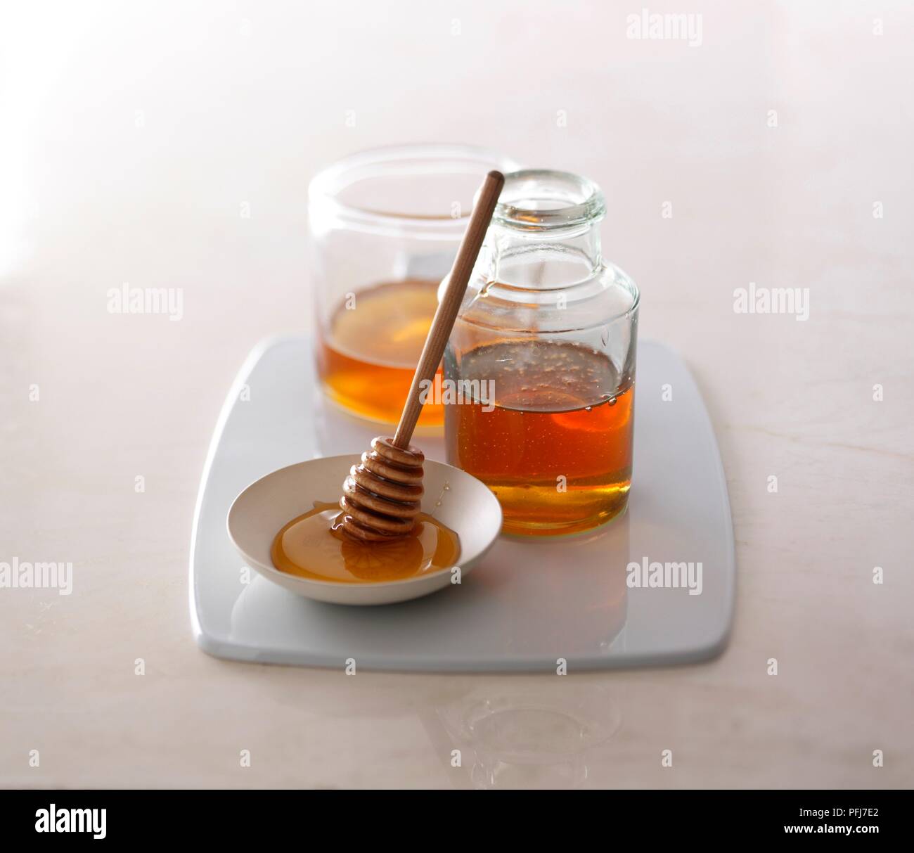 Two honey jars next to small dish of honey with honey dipper Stock ...