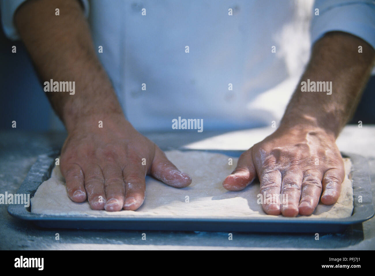 Pizza dough being patted out on rectangular baking tray Stock Photo - Alamy