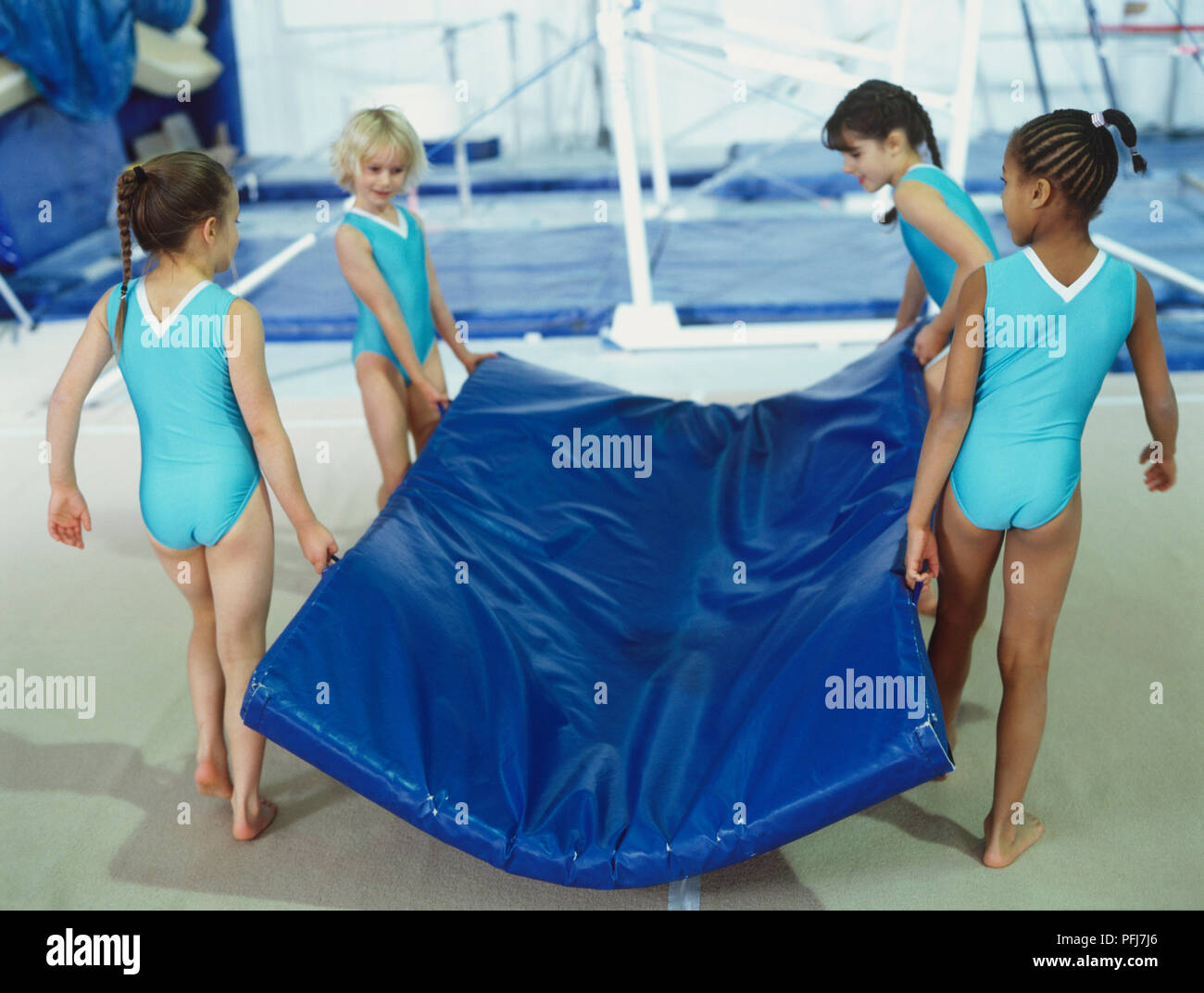 Four girls in gymnastics outfit, carrying heavy blue training mat Stock ...
