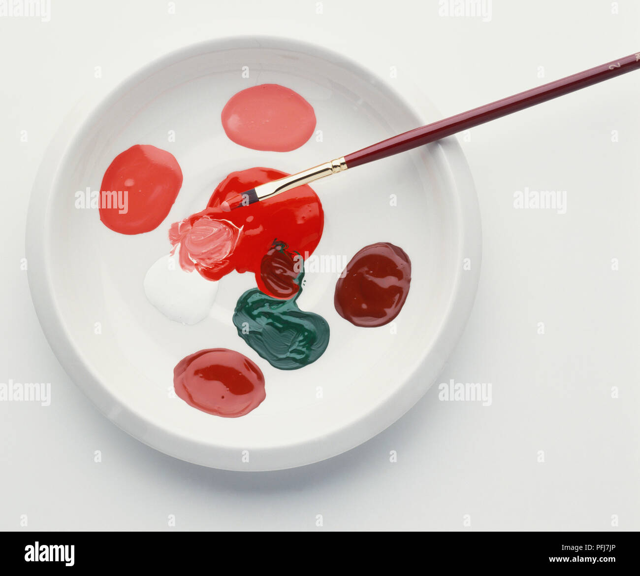Blobs of different coloured paint on white plate, fine brush mixing red ...