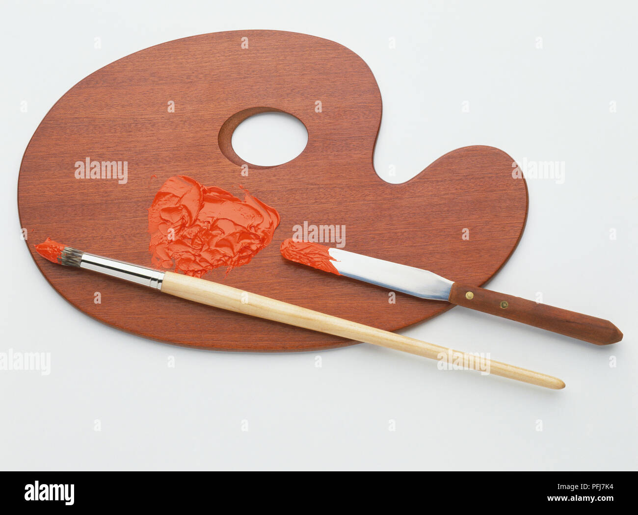 Wooden palette with blob of red paint, brush and mixing knife dipped in ...