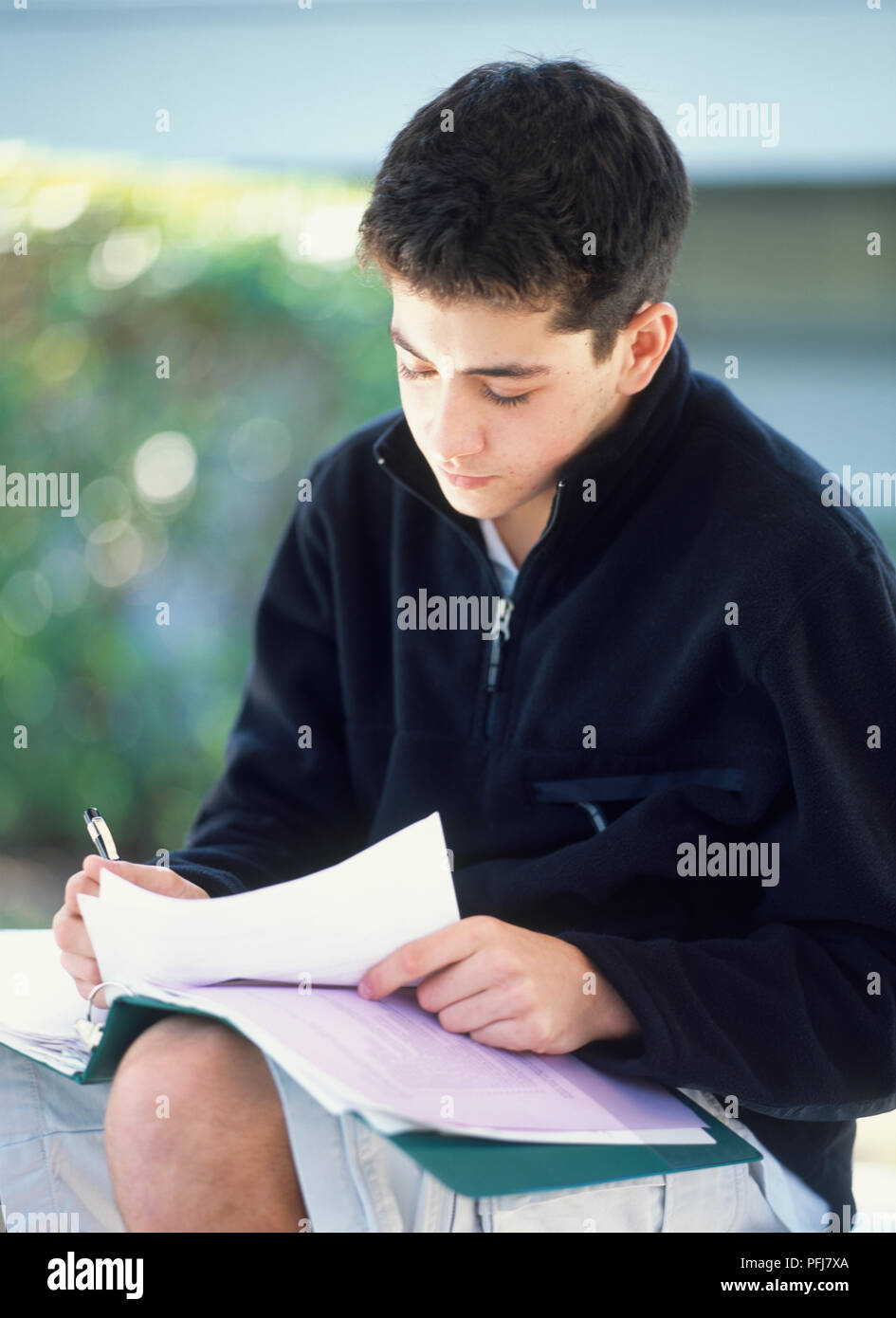 Boy sitting with a folder on his lap, taking notes Stock Photo - Alamy