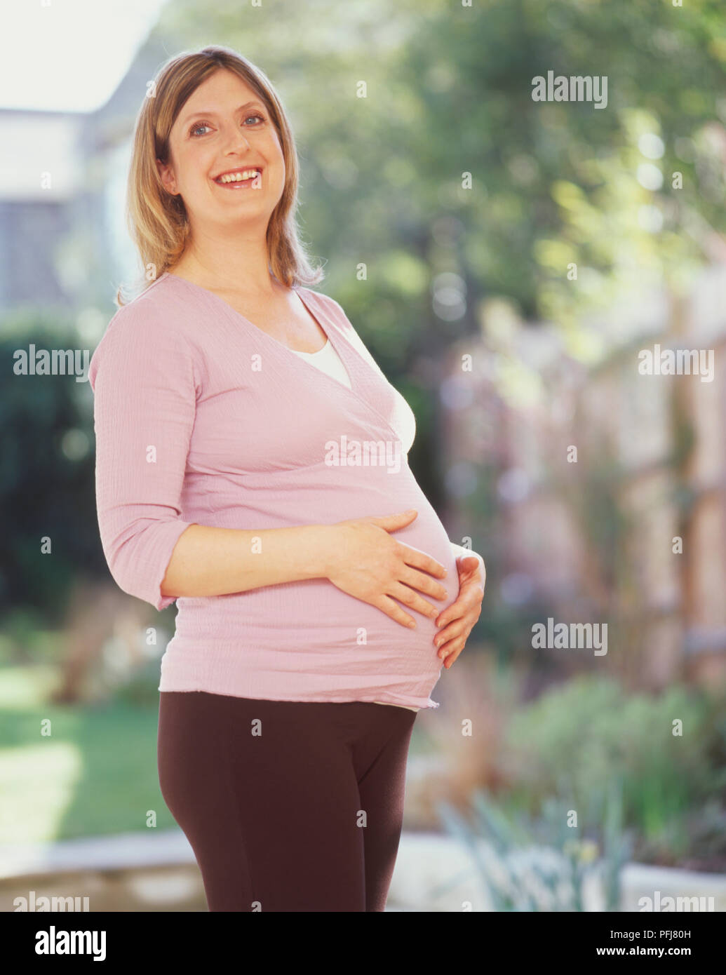 Woman resting her hands on swollen tummy and smiling Stock Photo - Alamy