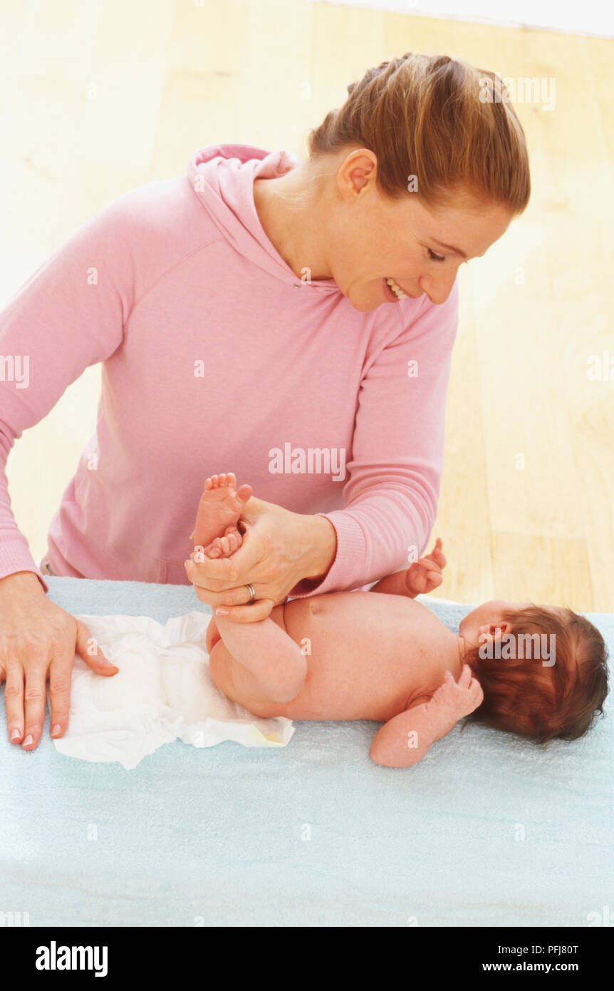 Woman smiling down at young baby, while holding both her feet in her ...