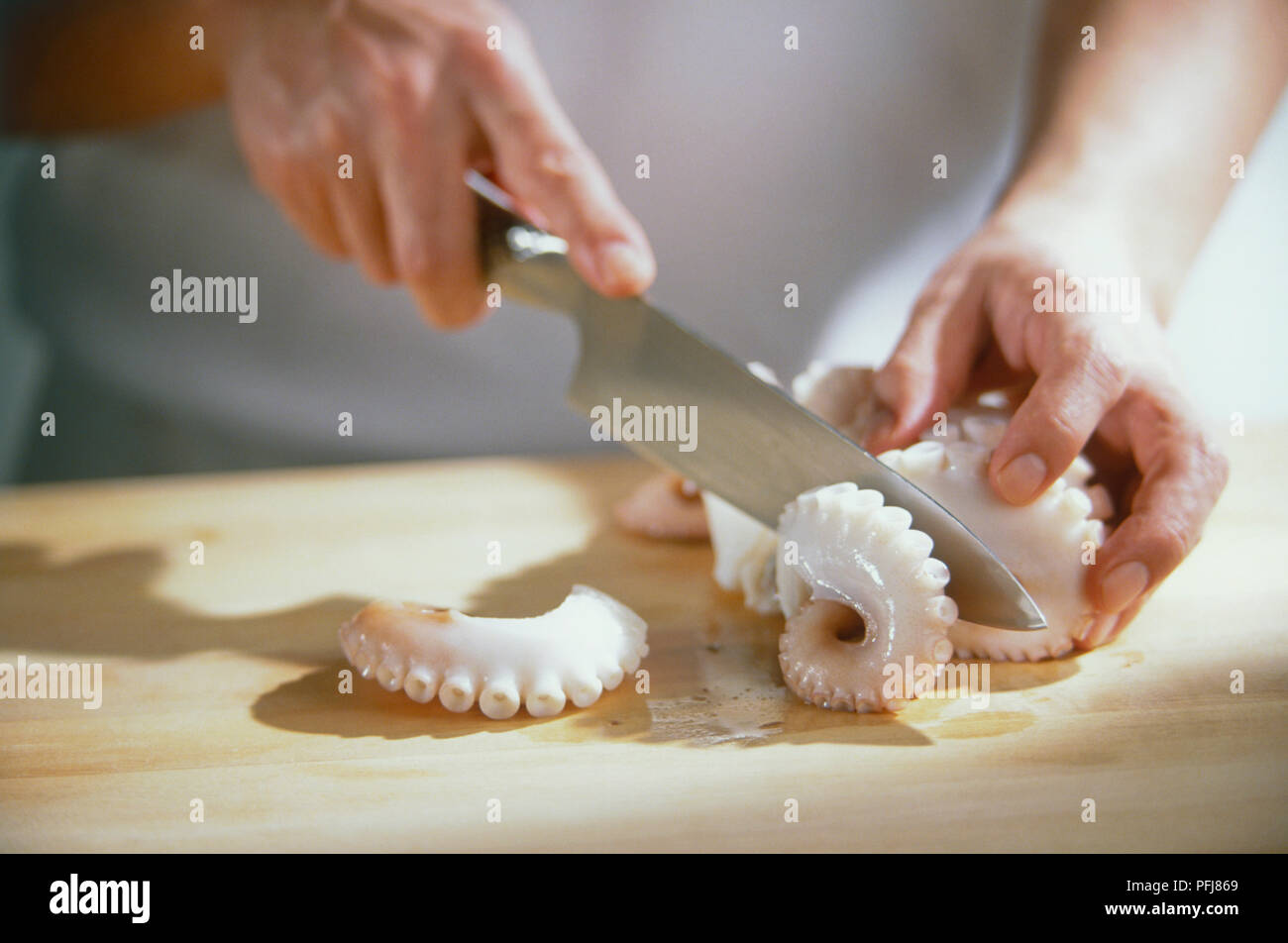 Hand holding kitchen knife to cut octopus tentacles on wood chopping ...