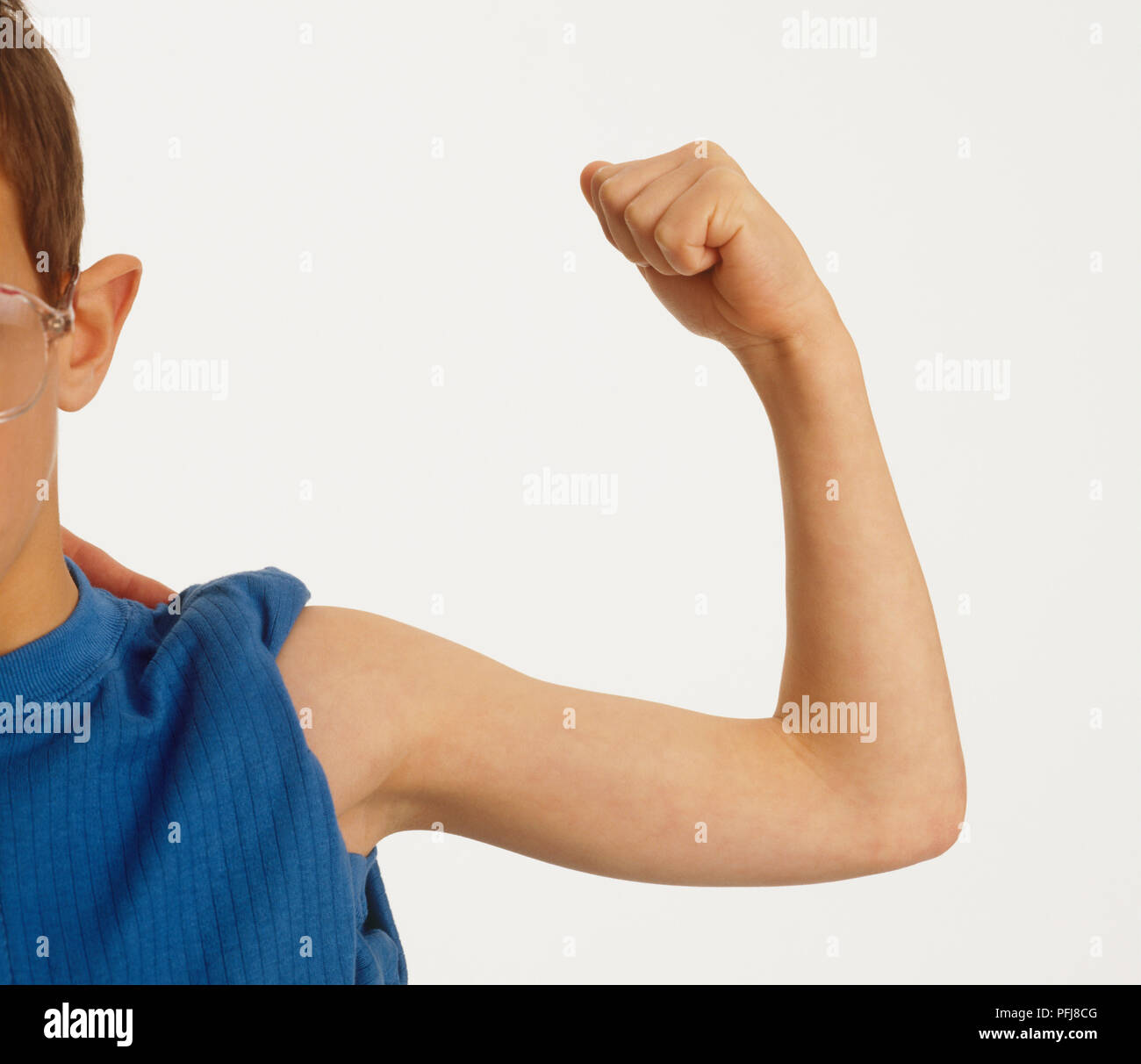 Boy with rolled up T-shirt sleeve making fist and flexing his arm ...