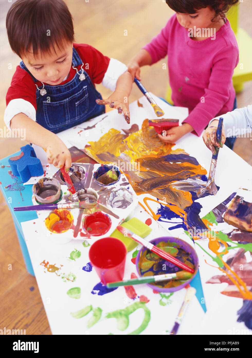 Three children around a table, dipping brushes in paint, painting, high ...
